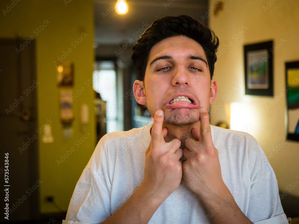 Young man pulling corners of lips down making unhappy facial expression ...
