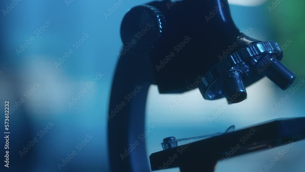 The camera moves across the microscope in a dark laboratory with soft blue light. Laboratory ...