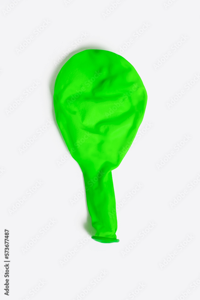 Deflated green balloon on a white isolated background. One uninflated ...