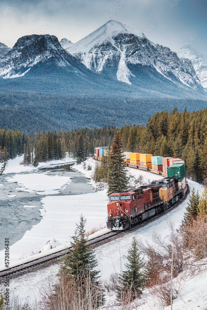 Morants Curve with iconic red cargo train passing through bow valley and rocky mountains in ...