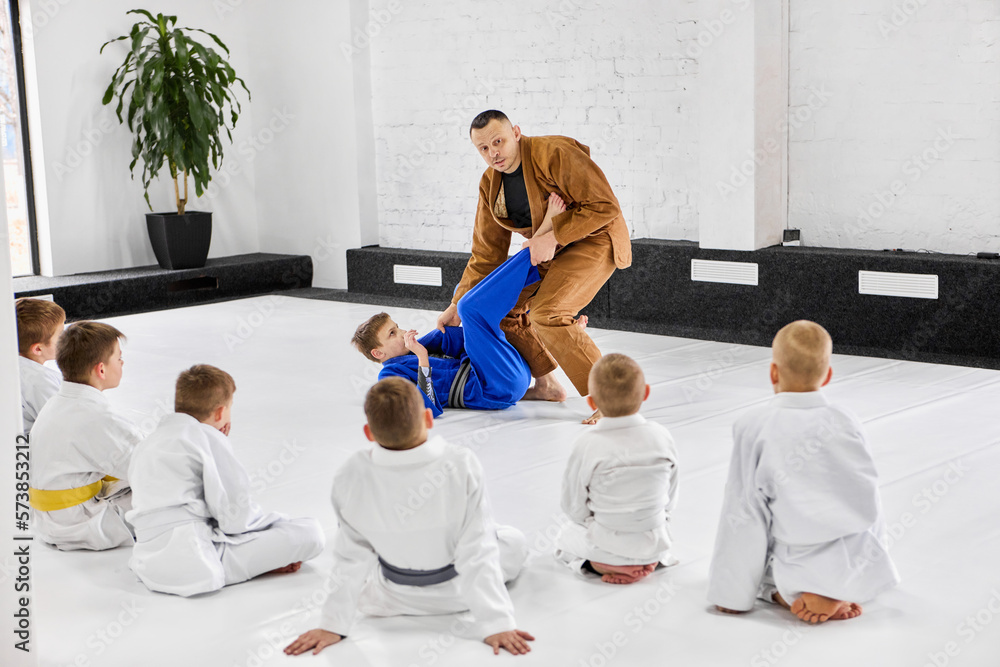 Teacher, judo, jiu jitsu coach training kinds, boys. Children learning indoors. Attentive look ...