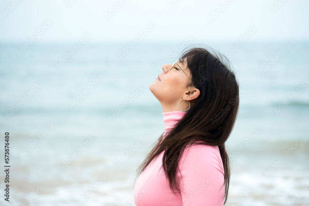 Woman in profile breathing fresh air in front of the sea in a pink ...