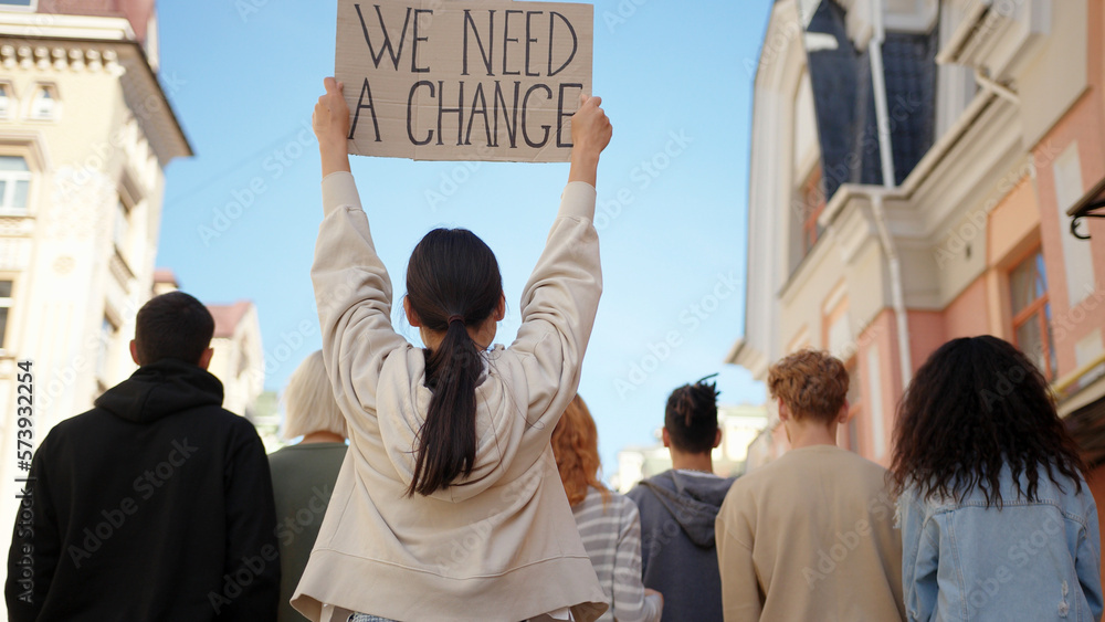 Asian woman in back of protest demonstration holding a poster We need a ...