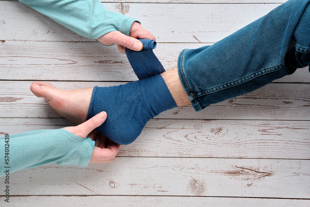 An adult wrapping compression bandage around sprained ankle of teenage ...