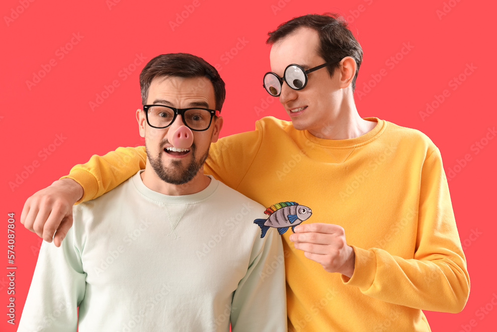 Young men in funny disguise with paper fish on red background. April ...