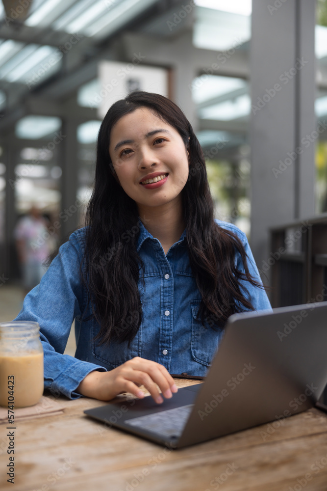 Portrait of a cute asian student girl coding IT laptop outdoors cafe and drinking a cup of ...