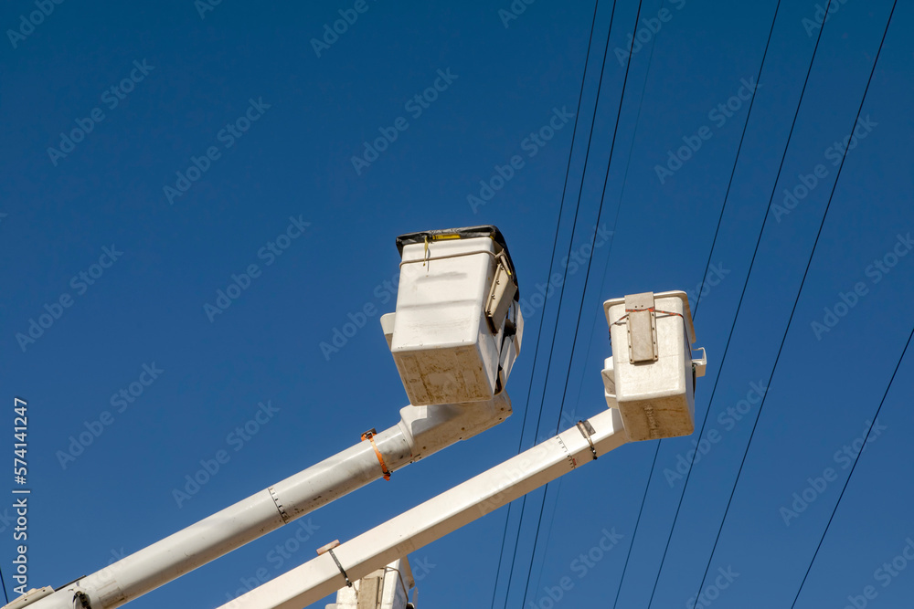 Manlift boom arms for utility work or trtee trimming against a blue sky ...