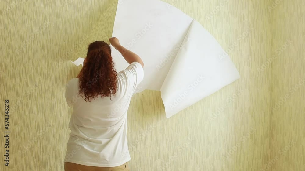 Curly red haired woman slowly pull and rip off old yellow wallpaper ...