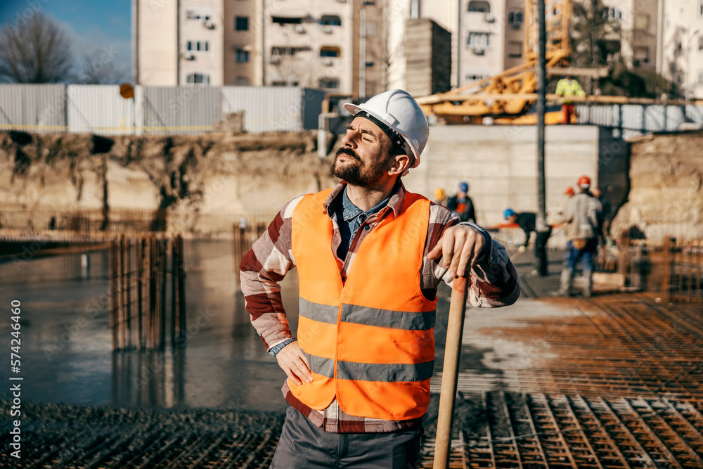 A hardworking builder is leaning on the shovel and taking a break from ...