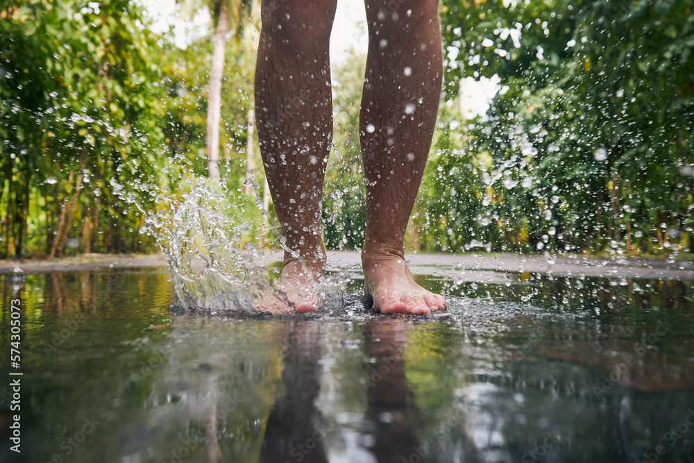 Man jumping with bare feet into puddle during rainy day. Close-up of ...
