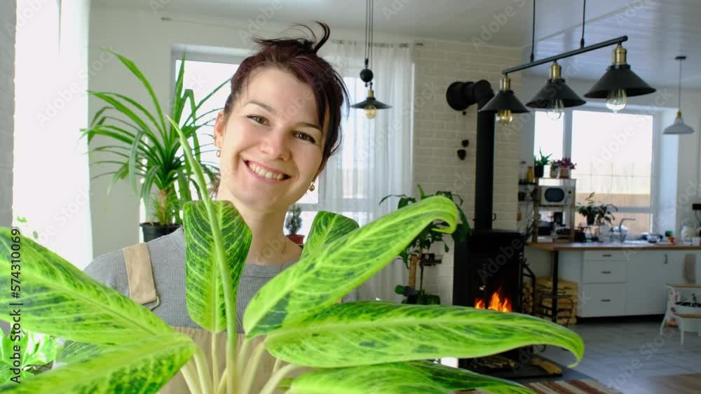A happy woman in a green house with a potted plant in her hands smiles ...