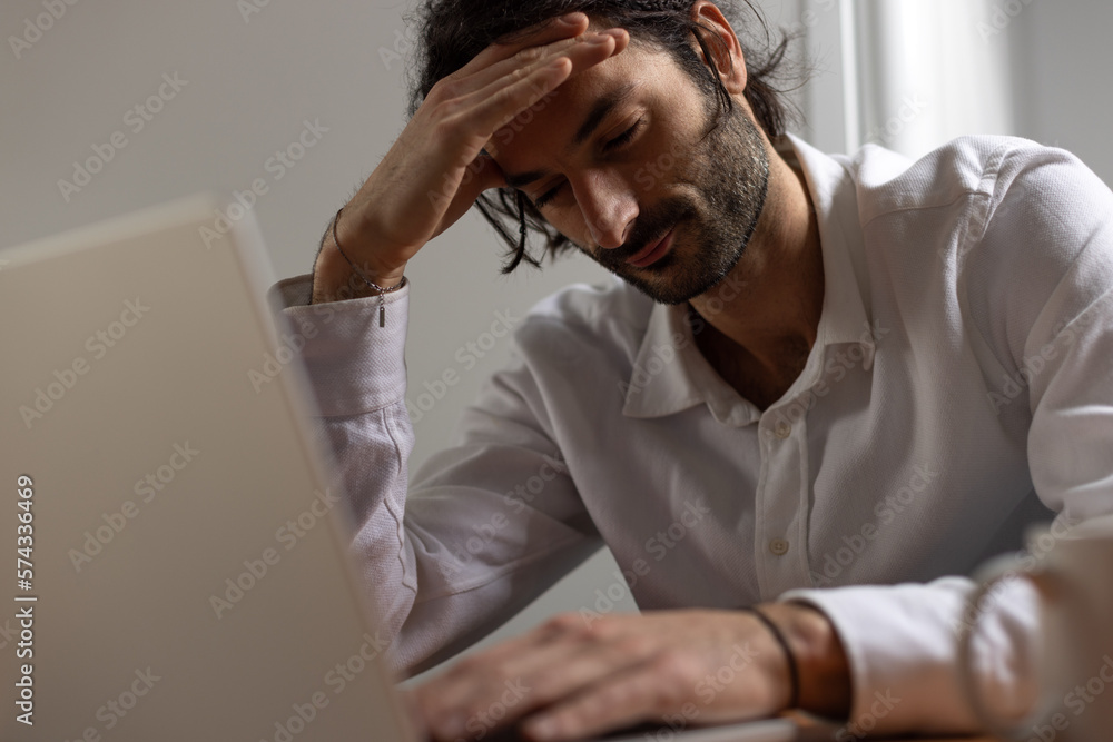 portrait d'un jeune employé de bureau assis devant son ordinateur. Il est fatigué et stressé et ...