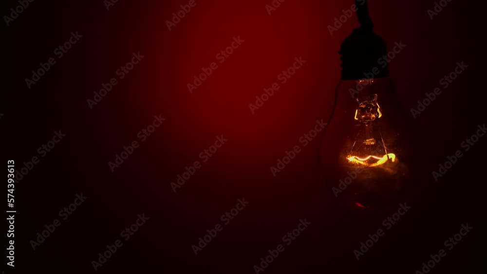 Light bulb flashes on a red background in the dark. Slow turning on and ...
