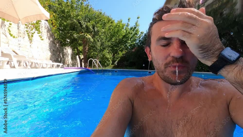 Smiling man jumping into the pool and resurfacing, straightening his ...