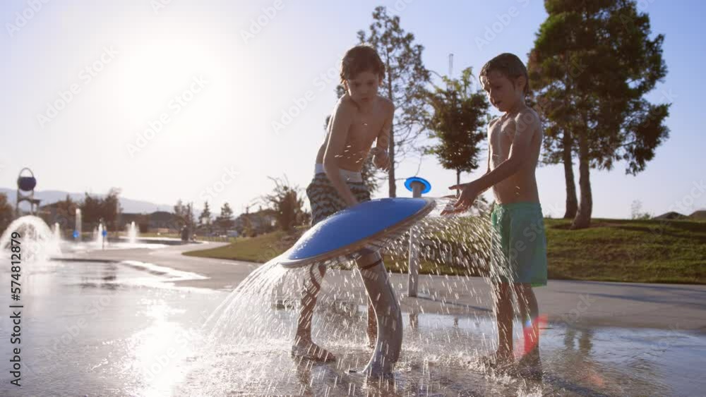 Two boys play with a spinning water feature at splash pad community ...
