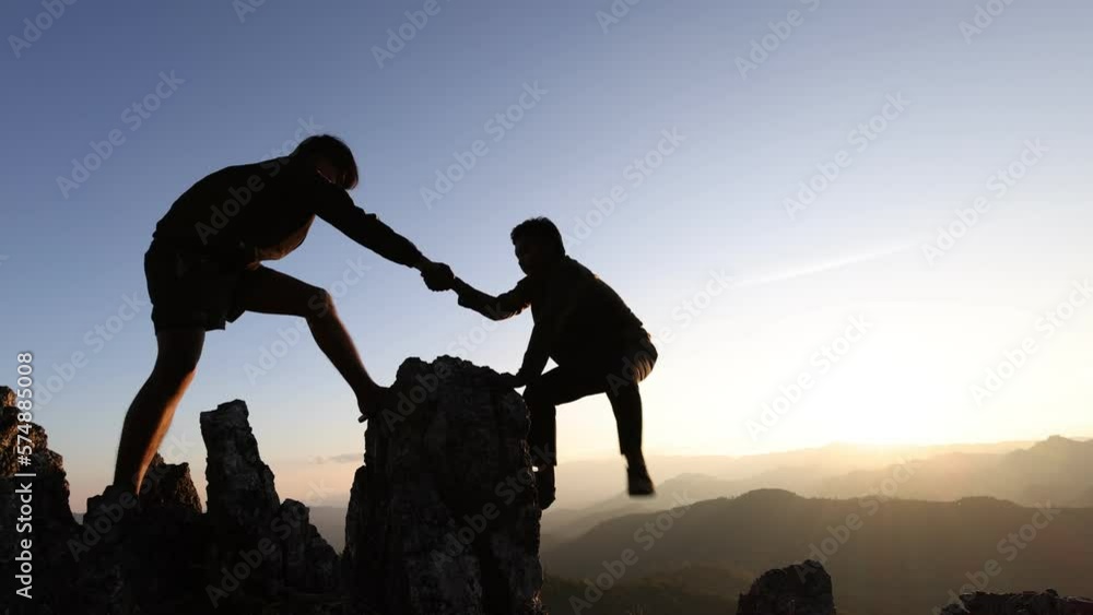 Silhouette of two tourists lends helping hand climb cliffs mountains ...