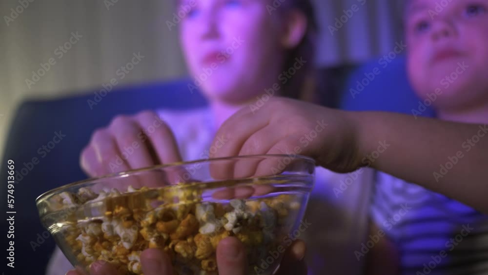 Plate of popcorn in hand. Sister girls are watching TV and eating ...