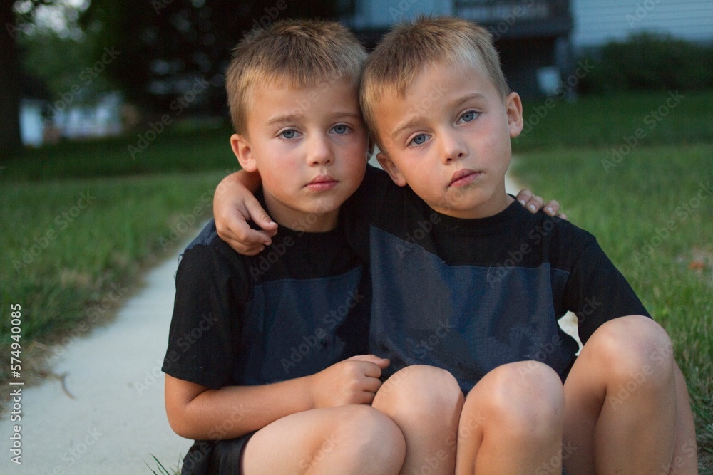 Portrait of twin brothers sitting on a street curb with their arms ...