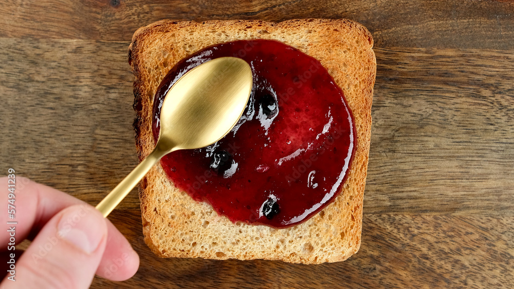 Blueberry jam spreading on bread with a golden spoon, top view. Perfect traditional breakfast ...