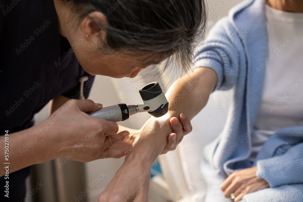 Female healthcare worker using a dermatoscope to check female patient's ...
