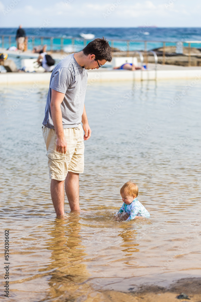 Happy young baby girl sitting in shallow sea water in ocean pool at ...