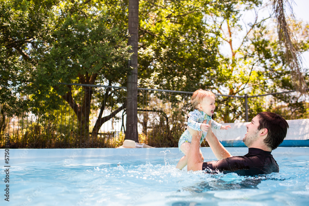 Father playing with baby in swimming pool dad lifting child high into ...