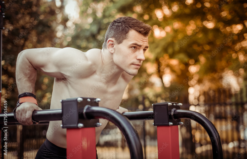 Athletic men with a naked torso do push-ups on the uneven bars on the ...