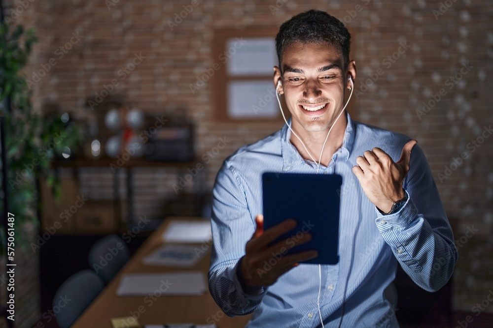 Handsome hispanic man working at the office at night pointing to the ...