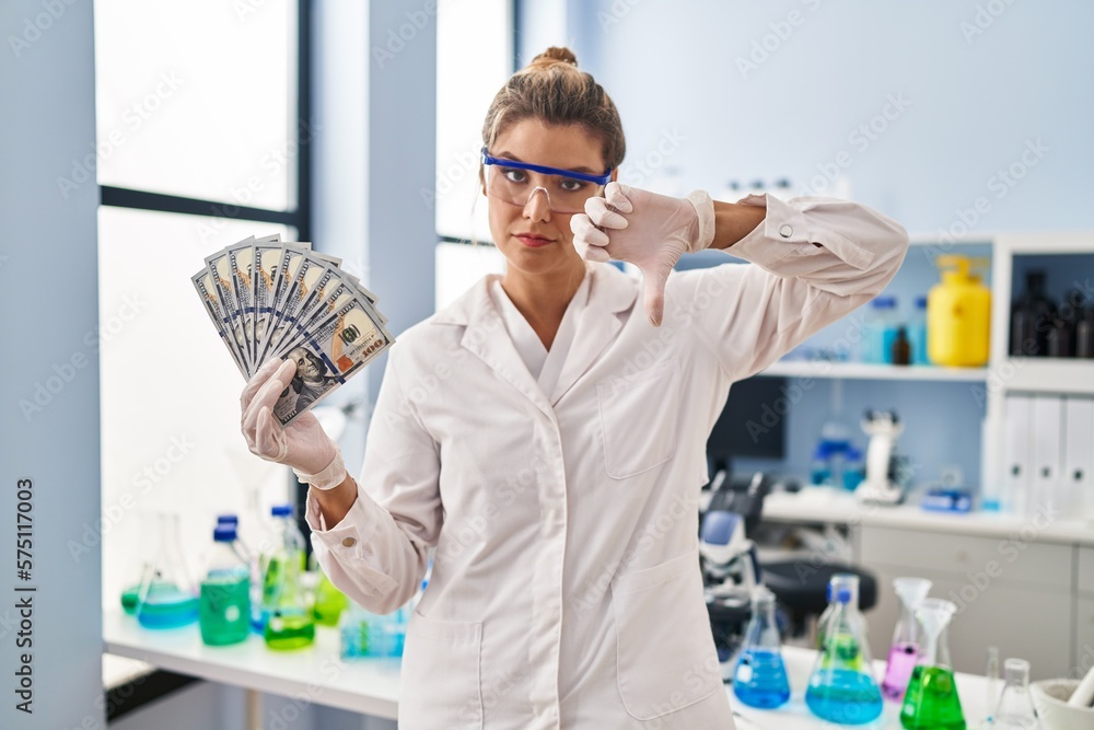 Young woman working at scientist laboratory holding money with angry ...