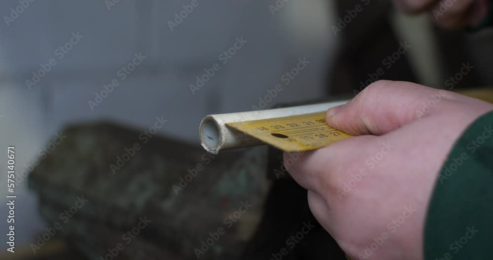 In a trowel, a man measures a piece of pipe with a ruler and makes a ...