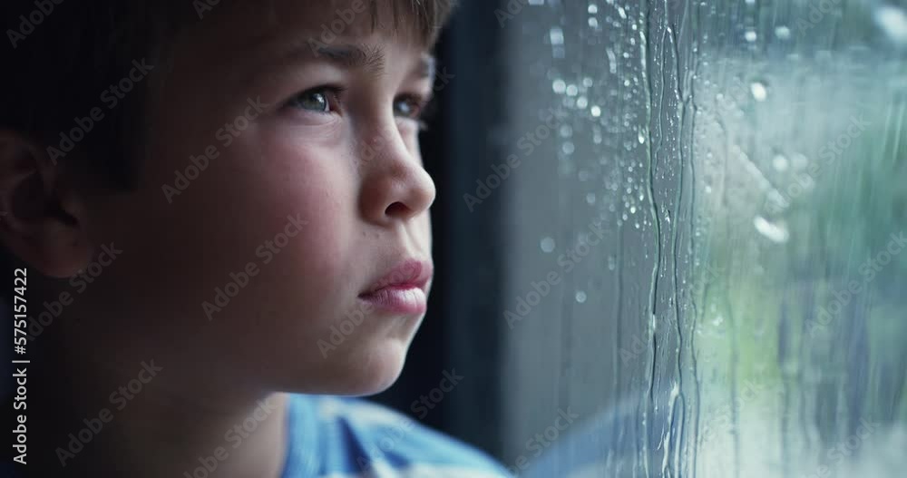A sad little boy depressed by bad weather, sitting inside watching rain ...