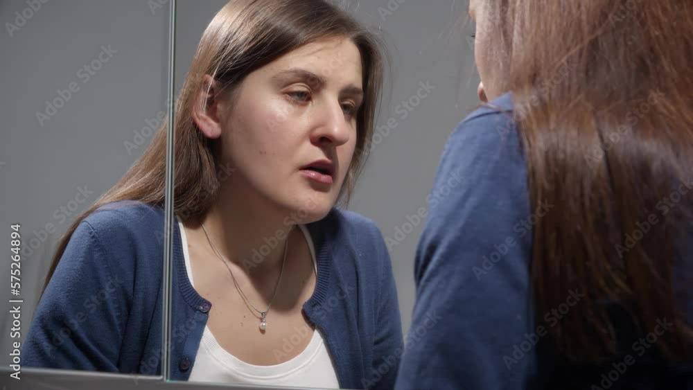 Stressed woman feeling unhappy standing at mirror and looking in ...