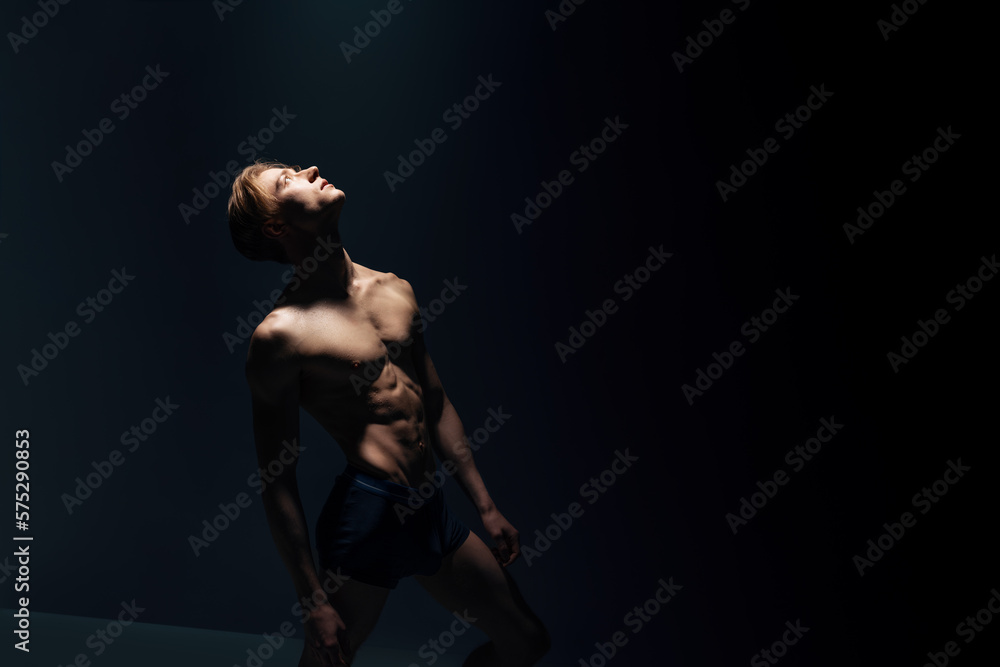 man in trunks stand in black studio and look up and pose in aesthetic ...