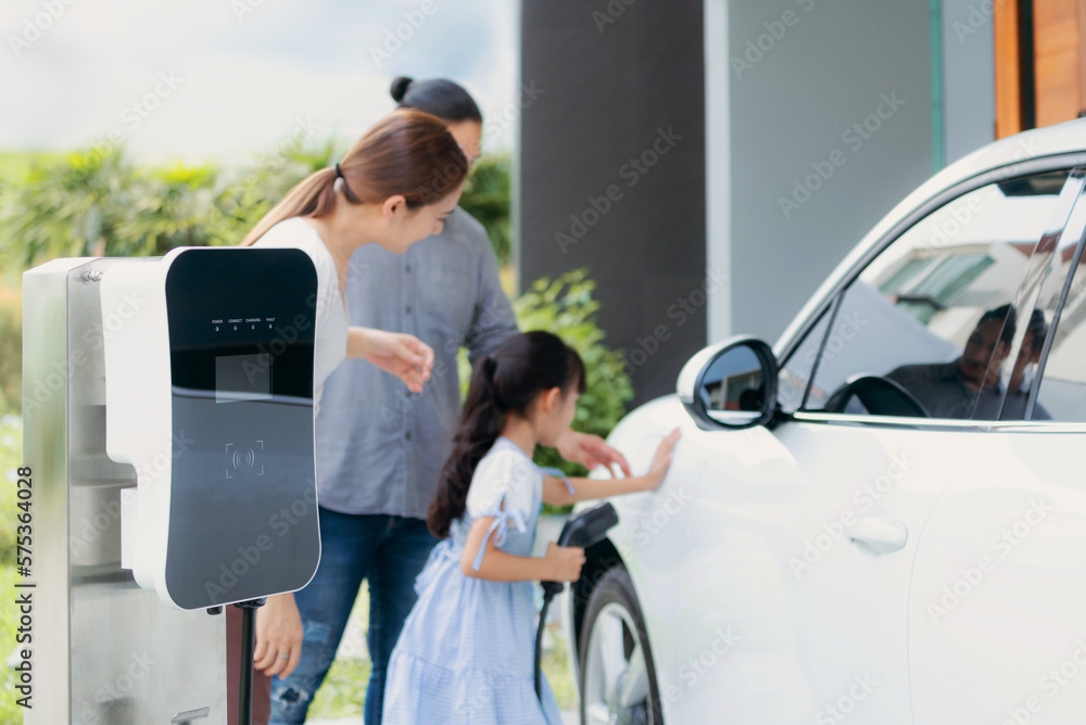 Progressive young parents and daughter with electric vehicle and home ...