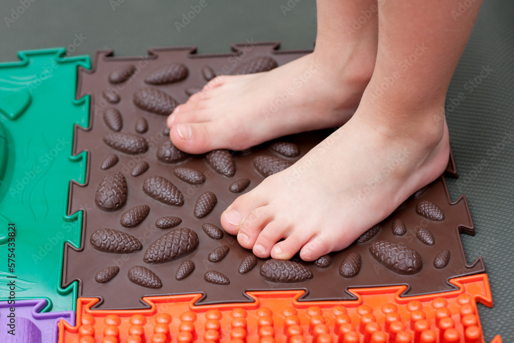 child does leg exercises on orthopedic massage mat at home. Puzzle mats ...