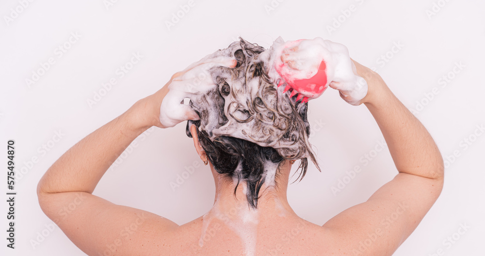 Lady with foam in her hair takes care of her scalp with pink massager ...