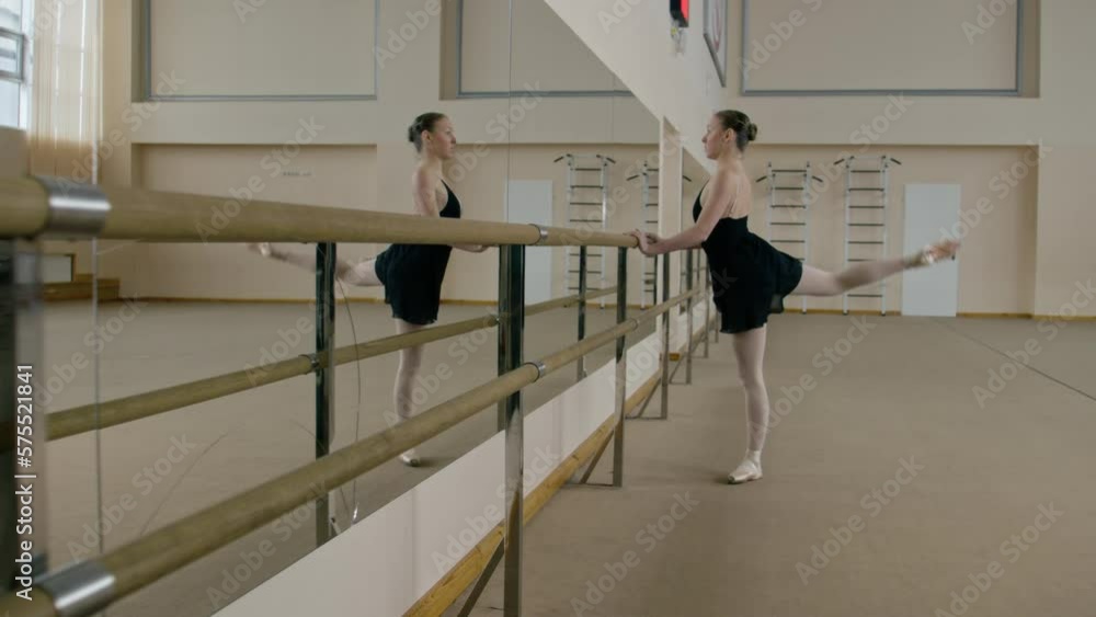Ballerina in training bodysuit stands in front of ballet barre at dance ...