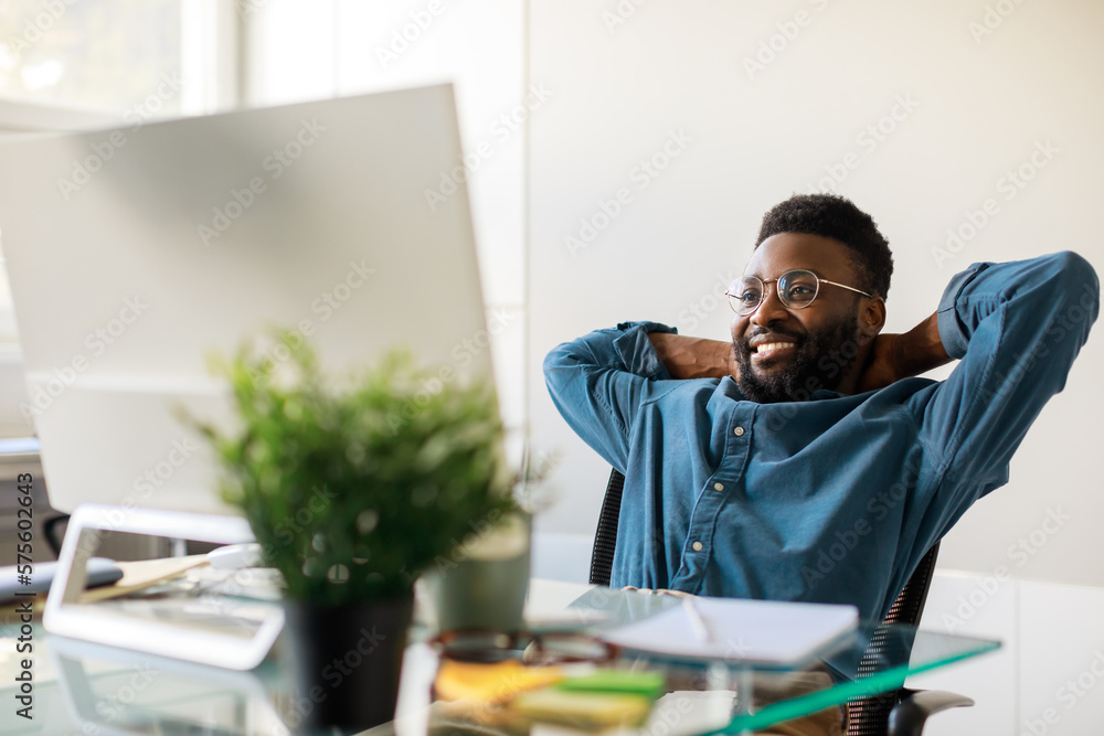 Positive black businessman holding hands behind head while sitting at ...