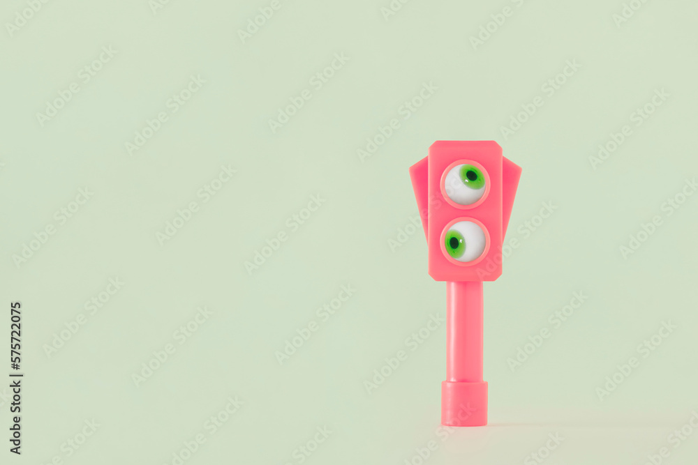 A coral pink traffic light looks around on an isolated pastel green ...