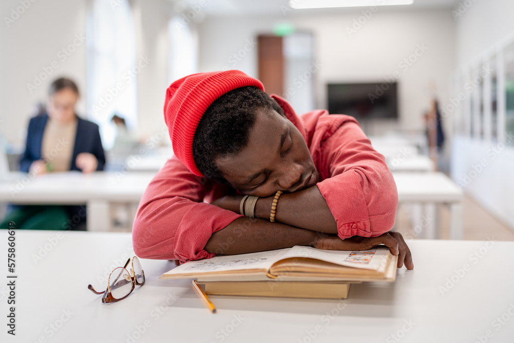 Lazy African male student falling asleep during study, feeling drowsy while studying in library ...