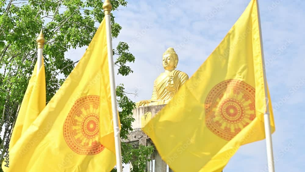 Golden Buddha statue with the Dhammacakka flag blowing by the wind. The ...