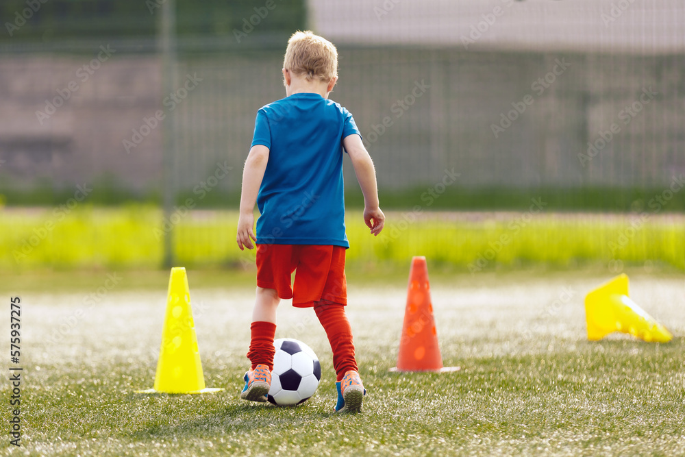 Lillte boy improving soccer skills by running the ball in slalom cones ...