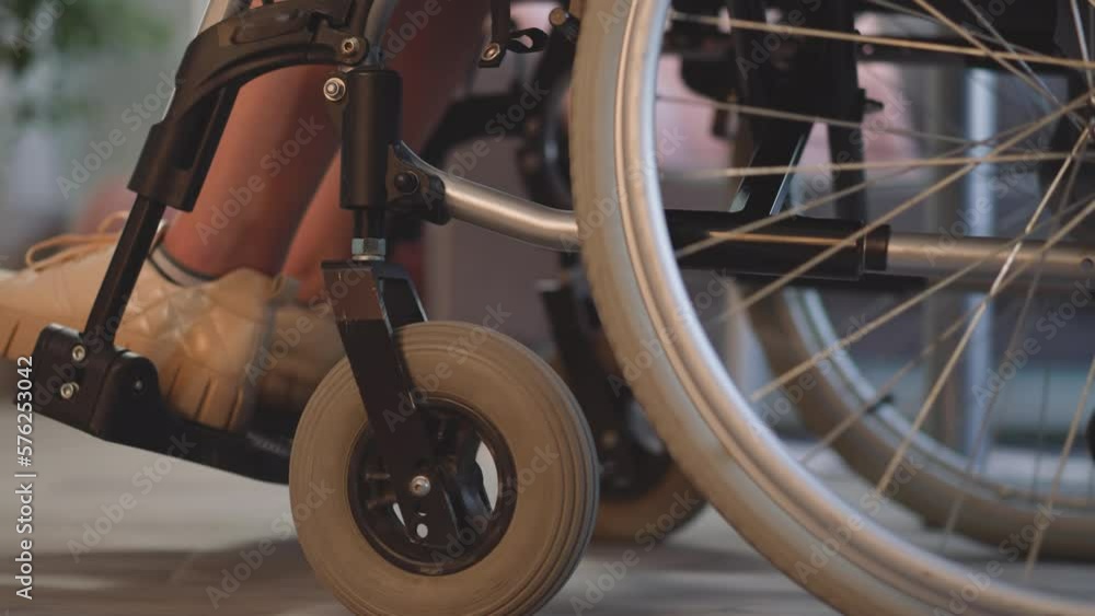 Legs of female patient with disability moving in wheelchair in room on ...