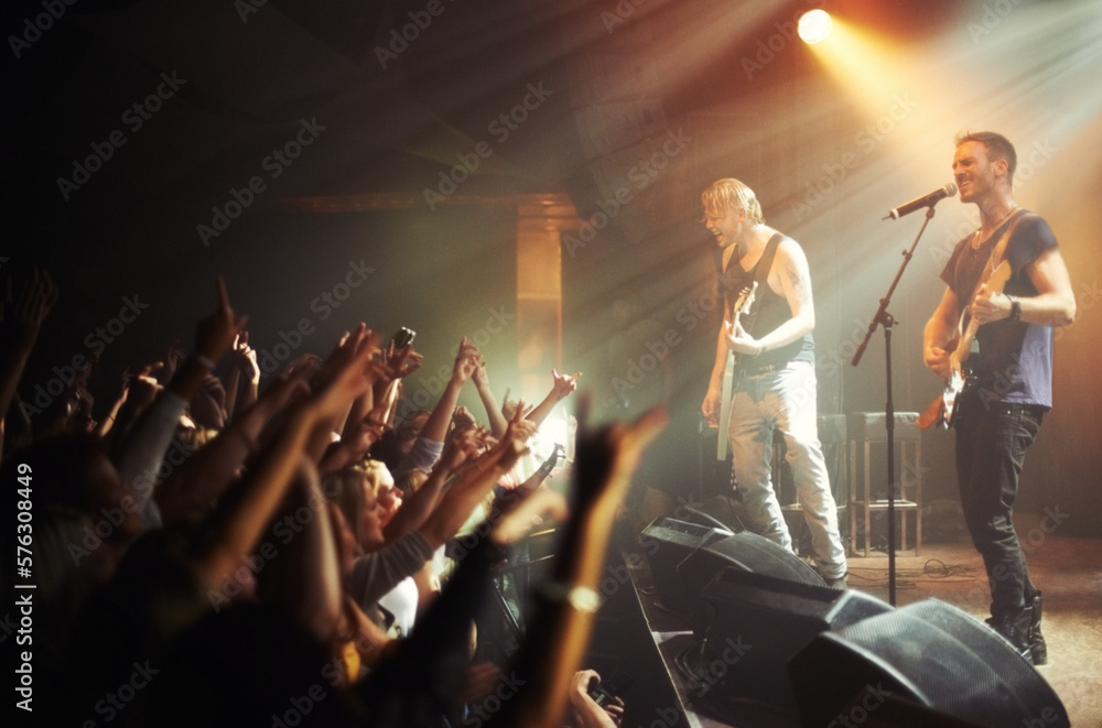 Shot of a crowd of music fans reaching up at a guitarist on stage. This ...