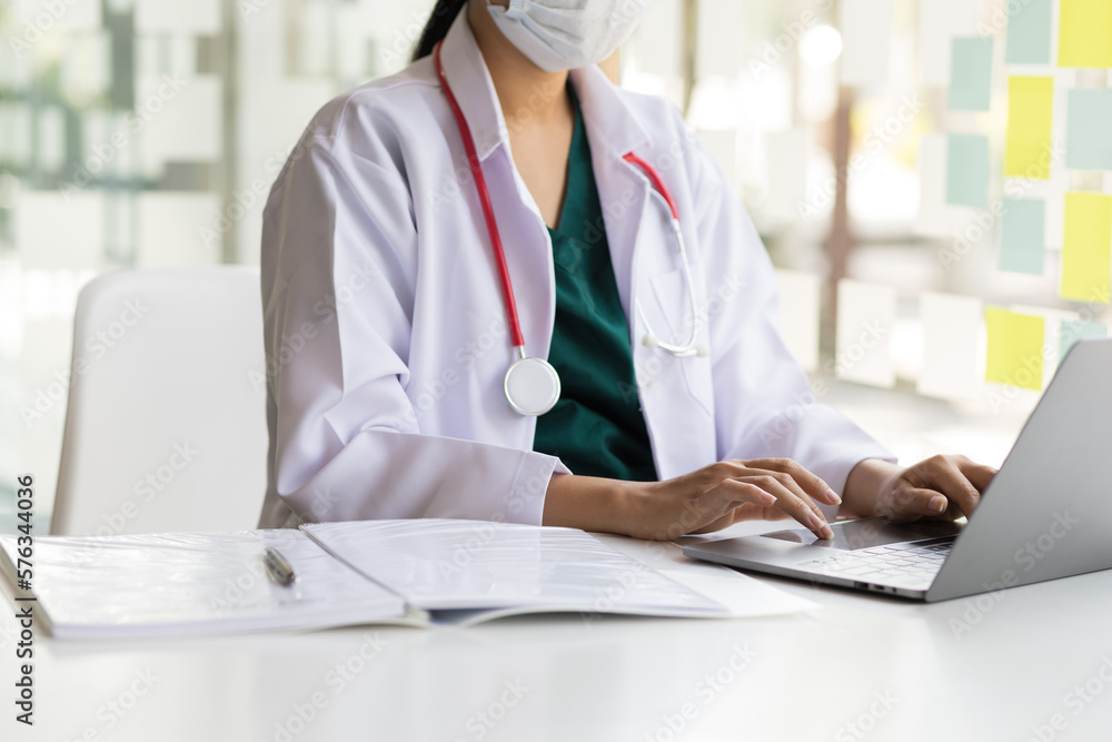 Female doctor checking patient history while working with laptop in ...