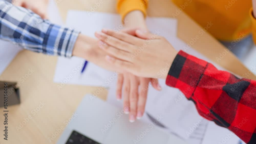 Colleagues put hands together on top of each other, say motto ...