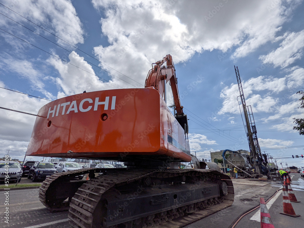 Constructing Progress: Hitachi Excavator and Workers on a Busy Street ...