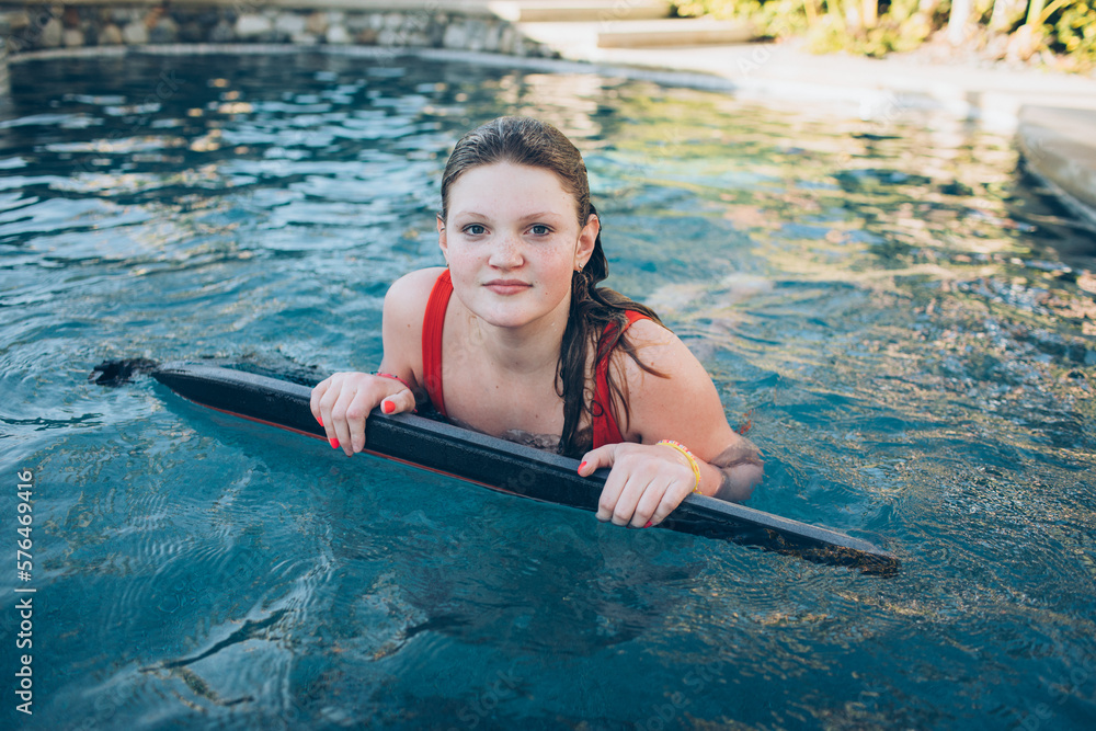 teenage girl with freckles and wet hair in red bathing suit in a pool ...