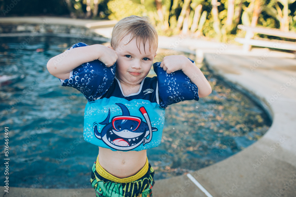 little boy wearing a lifejacket floaties making muscles in front of a ...