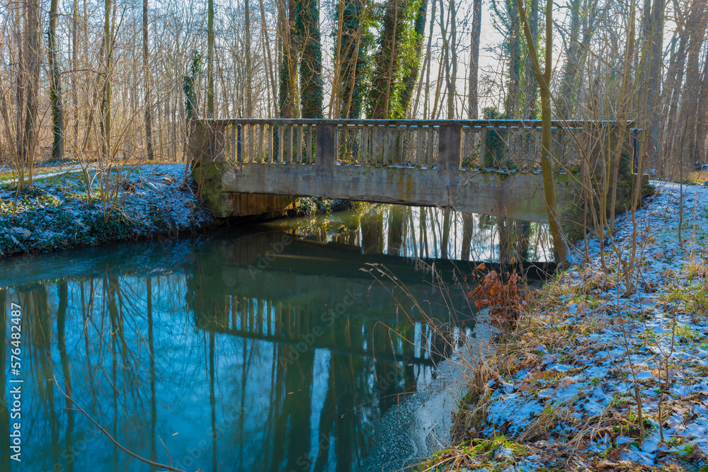 Small river in the forest in winter with a very old concrete bridge ...
